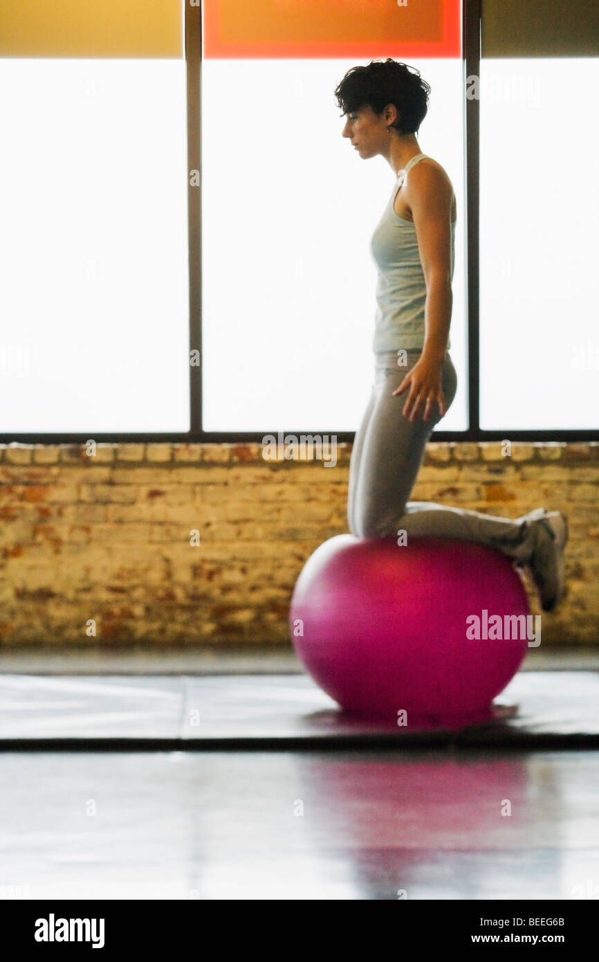 A young woman balancing atop an exercise ball while kneeling on it ...