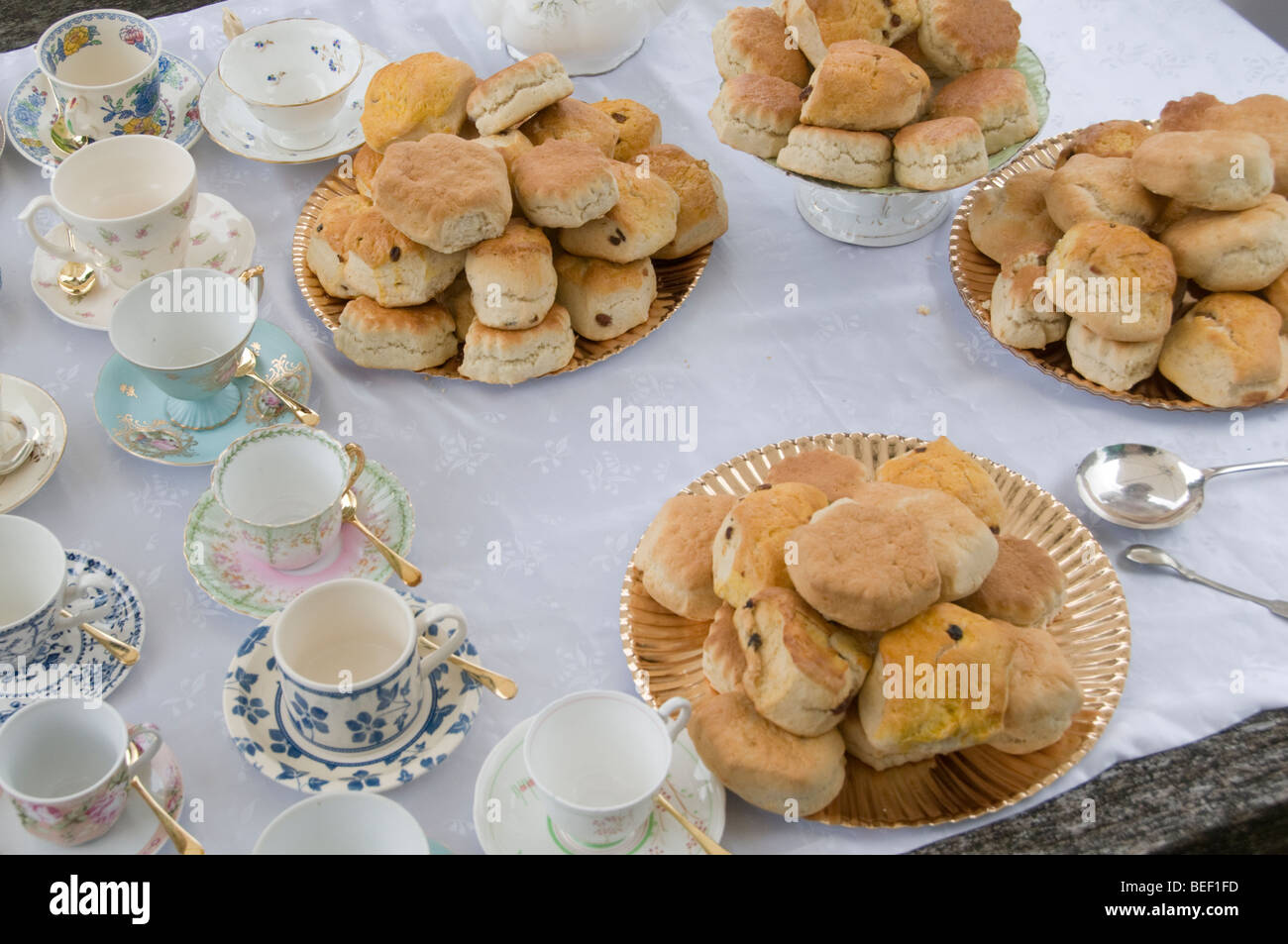 four plates of scones and colourful tea cups and saucers, on a table ...