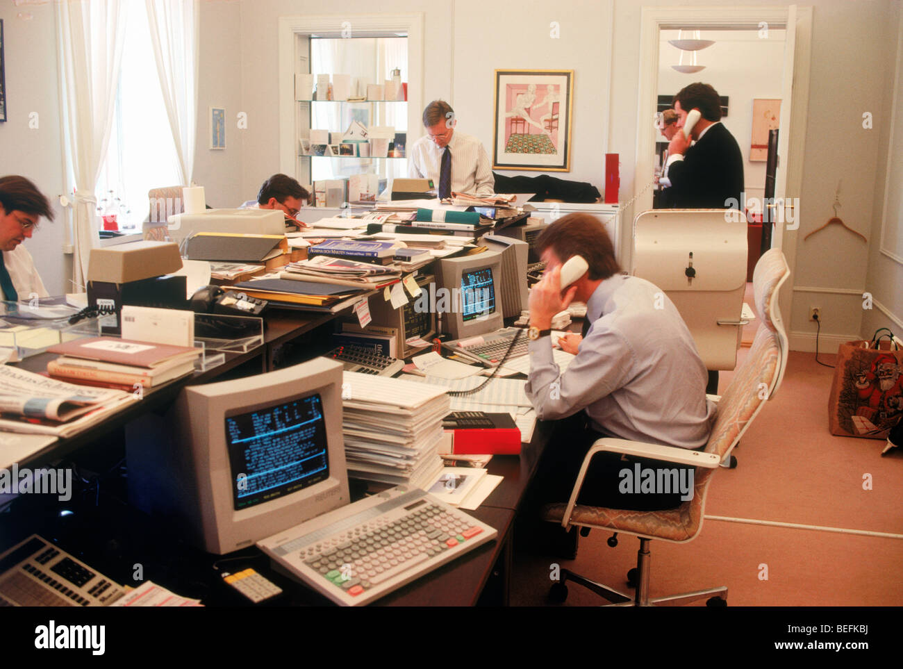 Businessmen and women busy talking on phones with computers on desktops ...