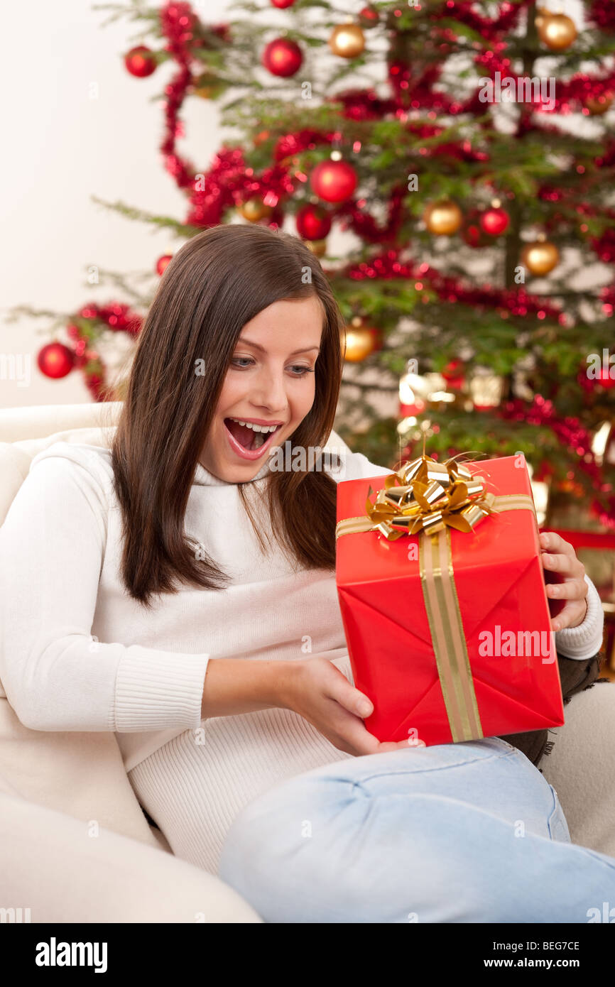 Surprised woman with Christmas gift in front of tree Stock Photo - Alamy