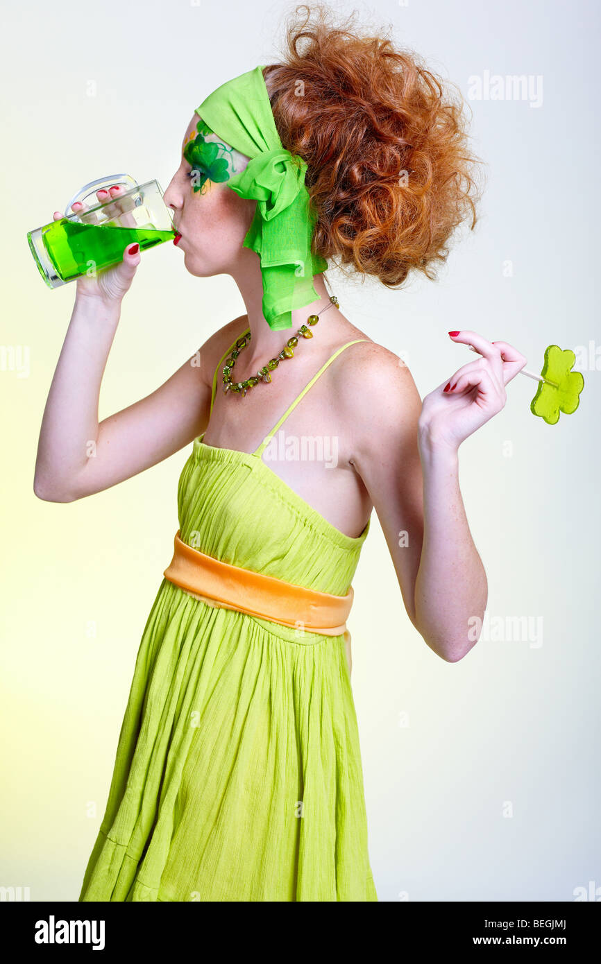 portrait of beautiful red-haired model with shamrock body art drinking ...