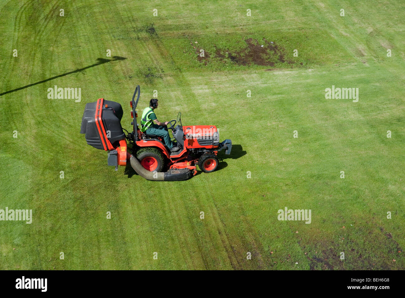 Man using petrol driven ride-on lawn mower to cut large area of grass ...