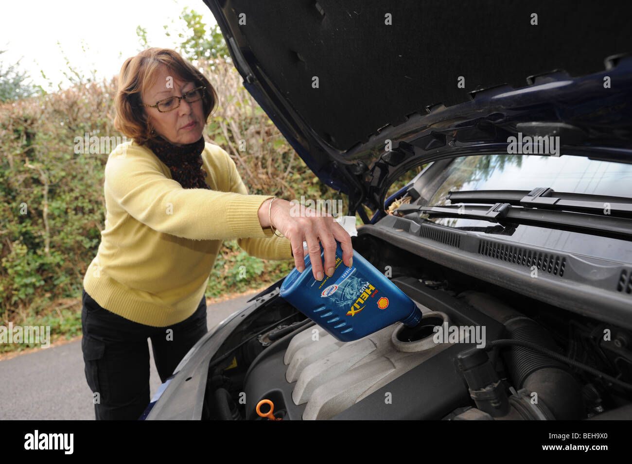 Woman driver topping up the oil in her car uk Stock Photo - Alamy