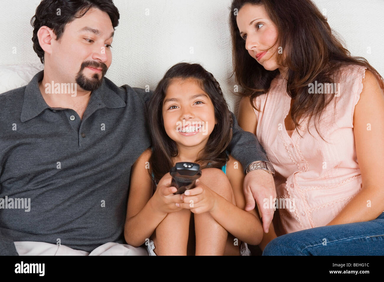 Portrait of a girl holding a remote control with her parents sitting ...