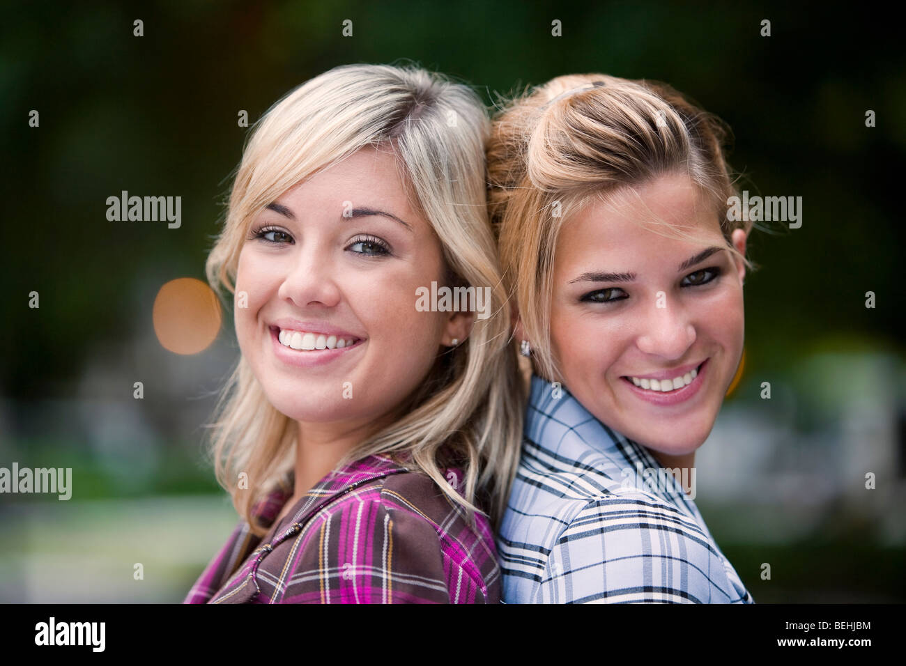 Portrait of two young women back to back and smiling Stock Photo - Alamy