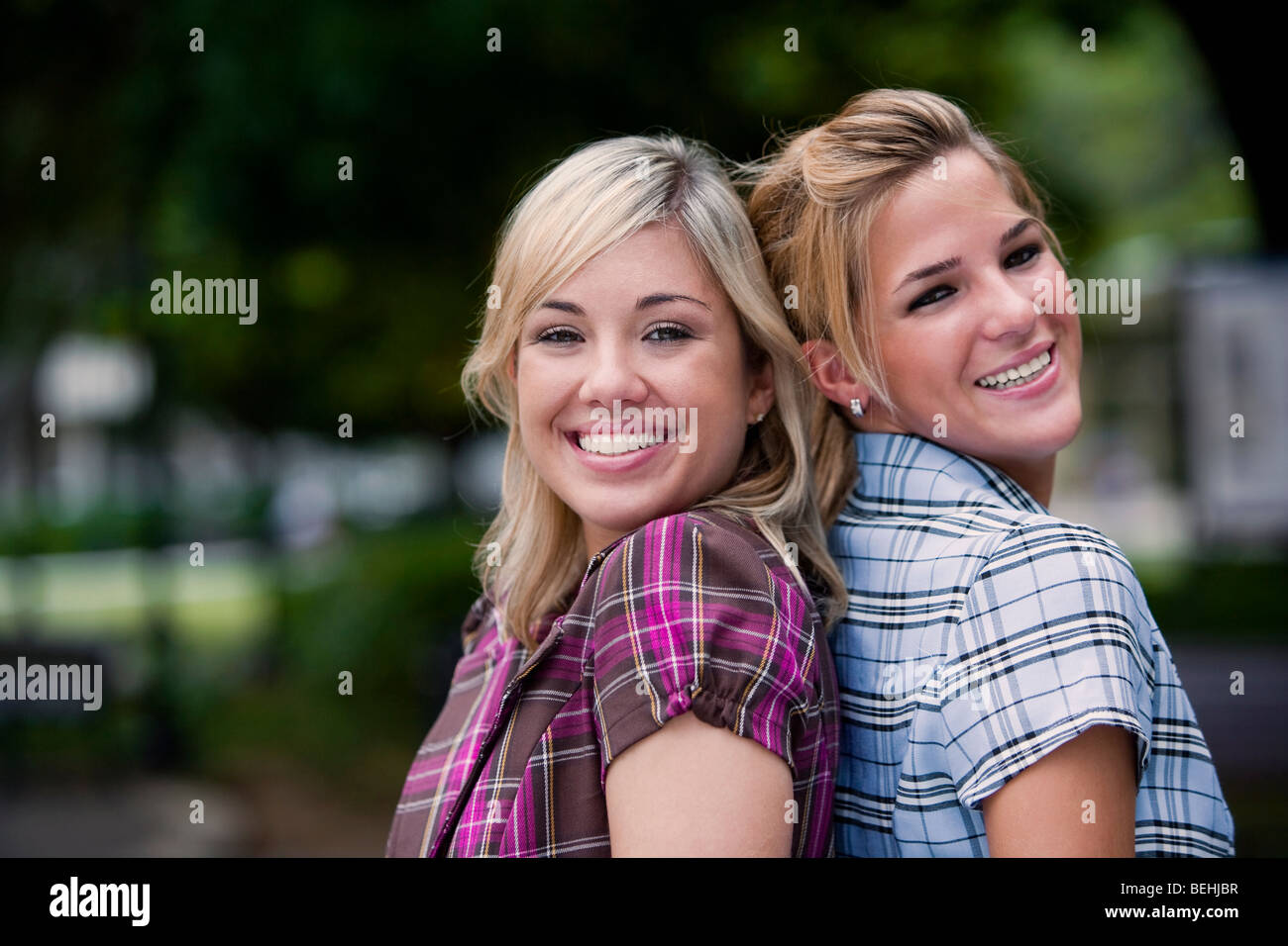 Portrait of two young women back to back and smiling Stock Photo - Alamy