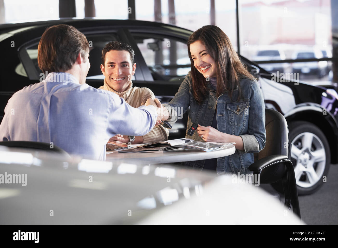 Rear view of a salesman shaking hand with a young woman in a car ...