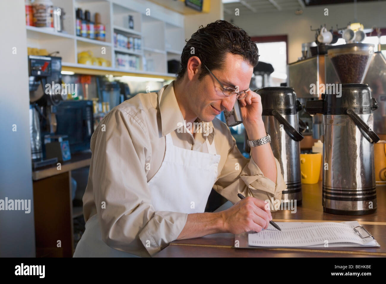 Male store clerk using a cordless phone and checking inventory Stock ...