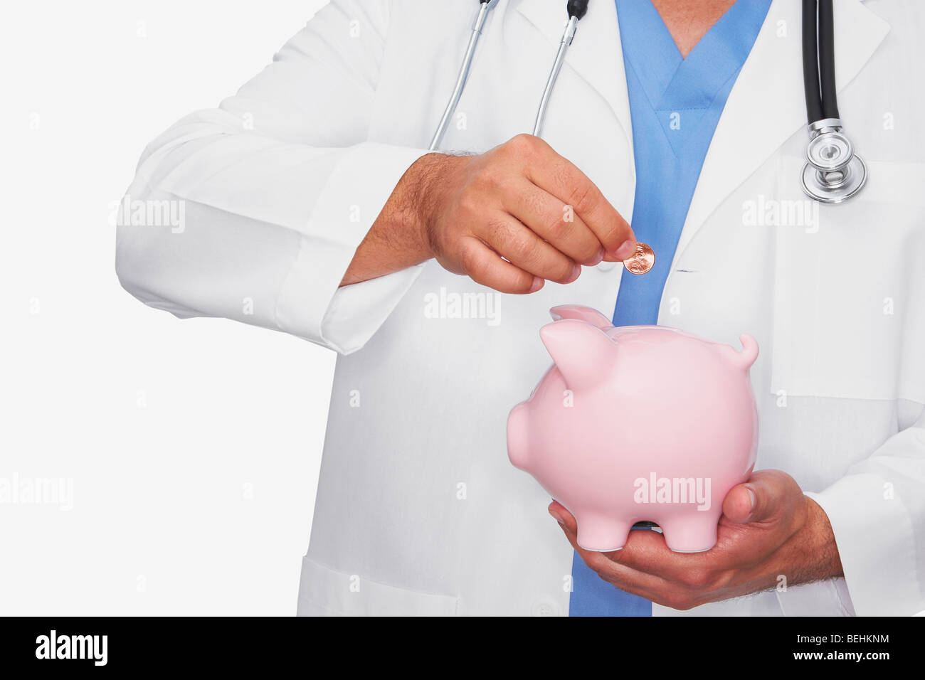 Mid section view of a male doctor inserting a coin into a piggy bank ...