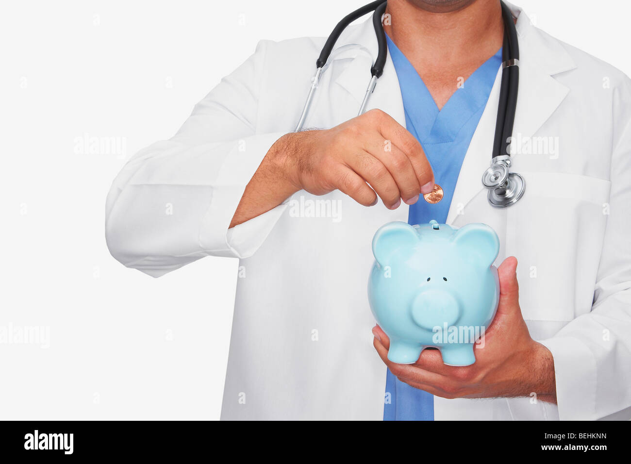 Mid section view of a male doctor inserting a coin into a piggy bank ...