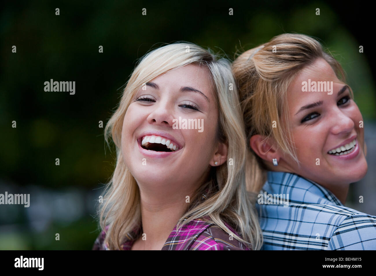 Portrait of two young women back to back and smiling Stock Photo - Alamy