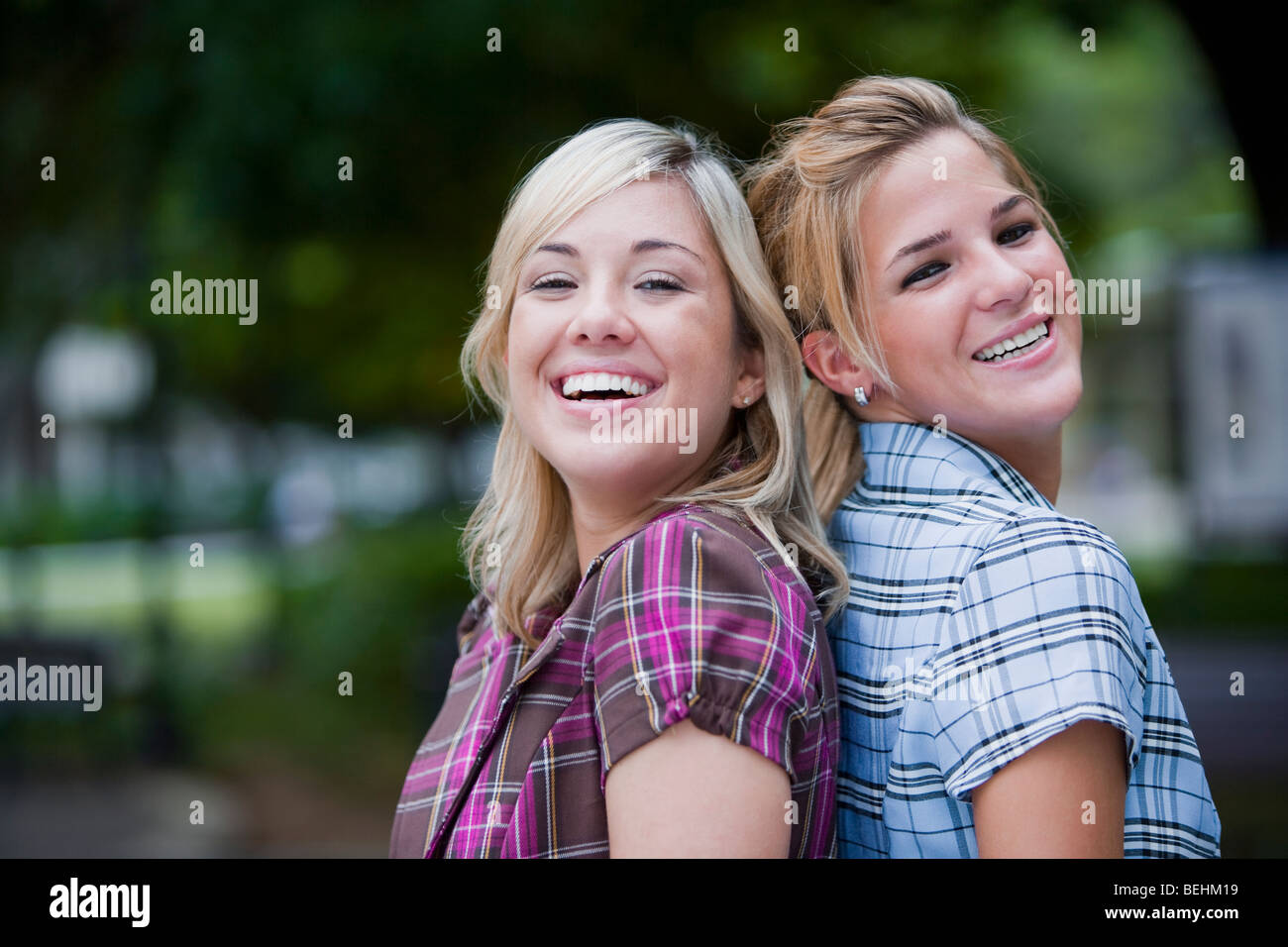 Portrait of two young women back to back and smiling Stock Photo - Alamy