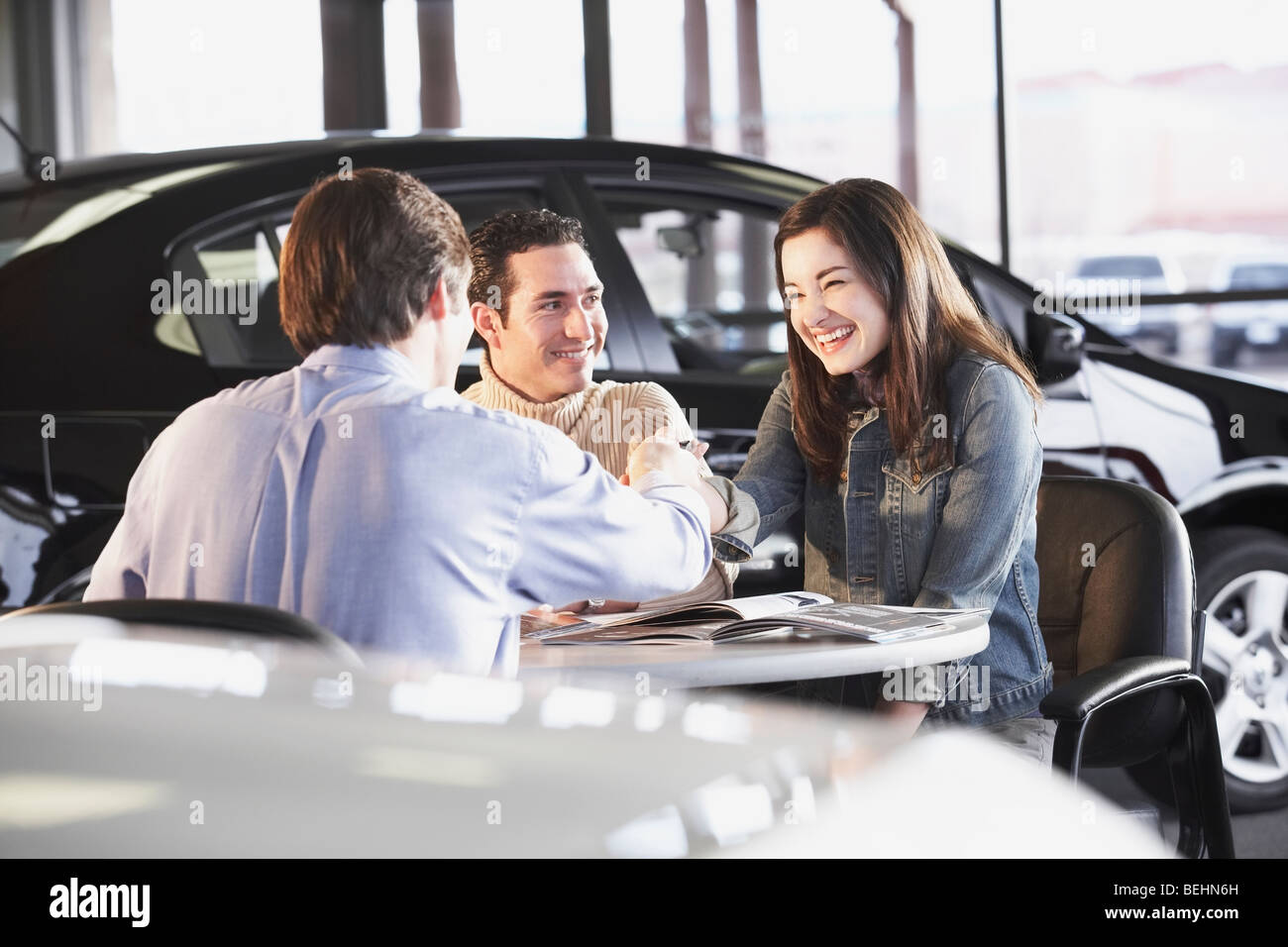 Rear view of a salesman talking to a couple in a car showroom Stock ...