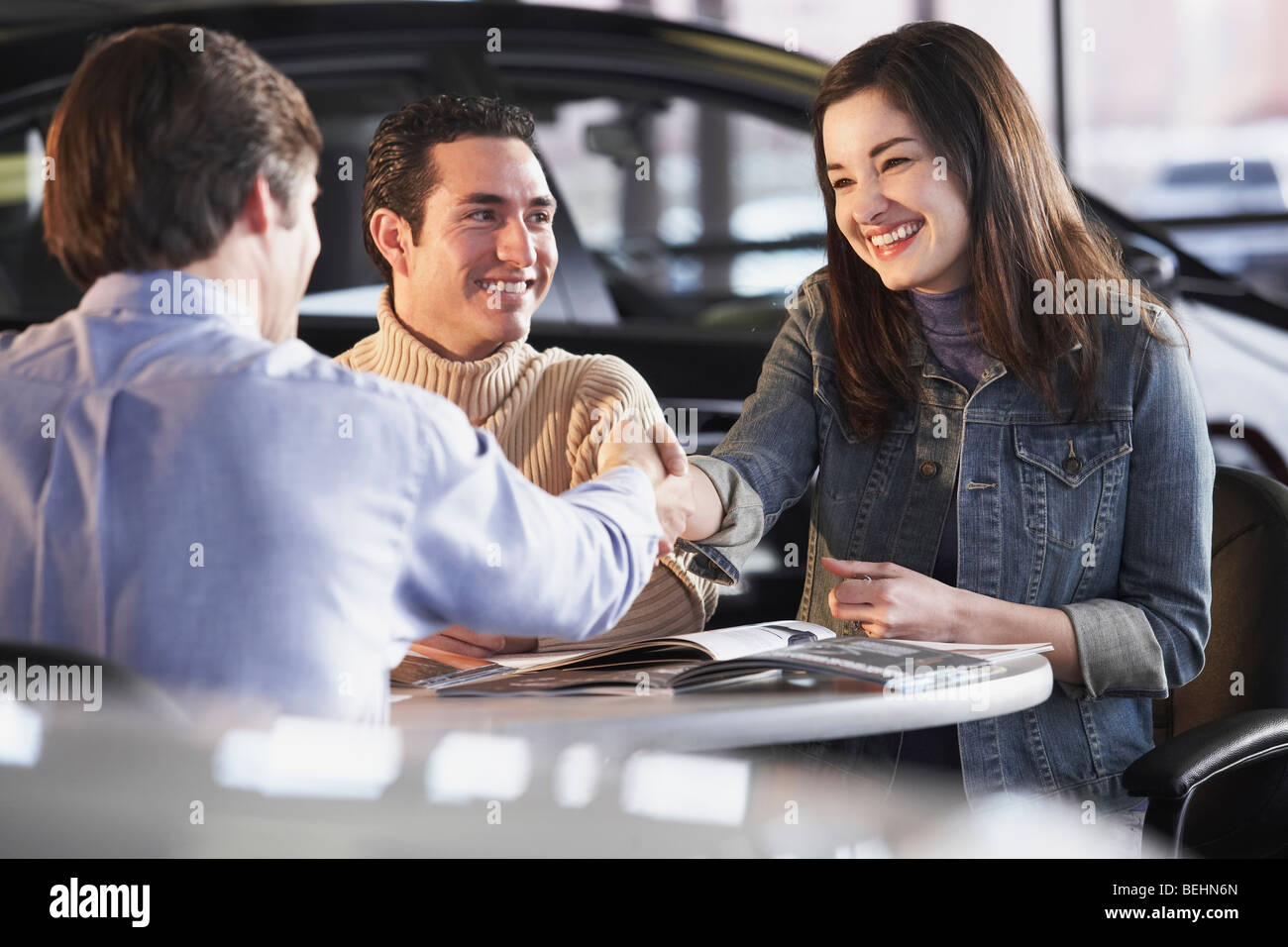Rear view of a salesman shaking hand with a young woman in a car ...