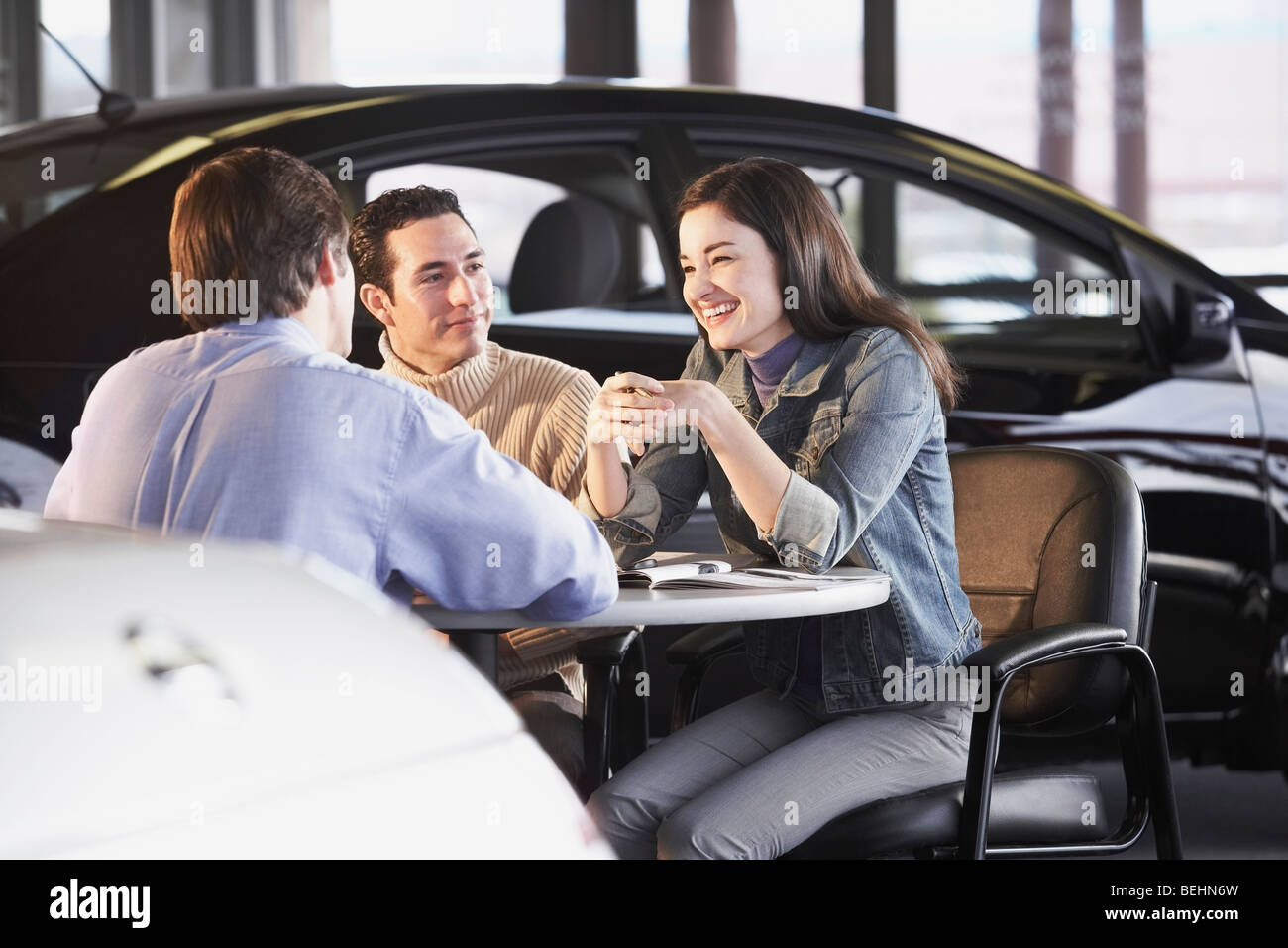 Rear view of a salesman giving details about a car to a couple in a car ...