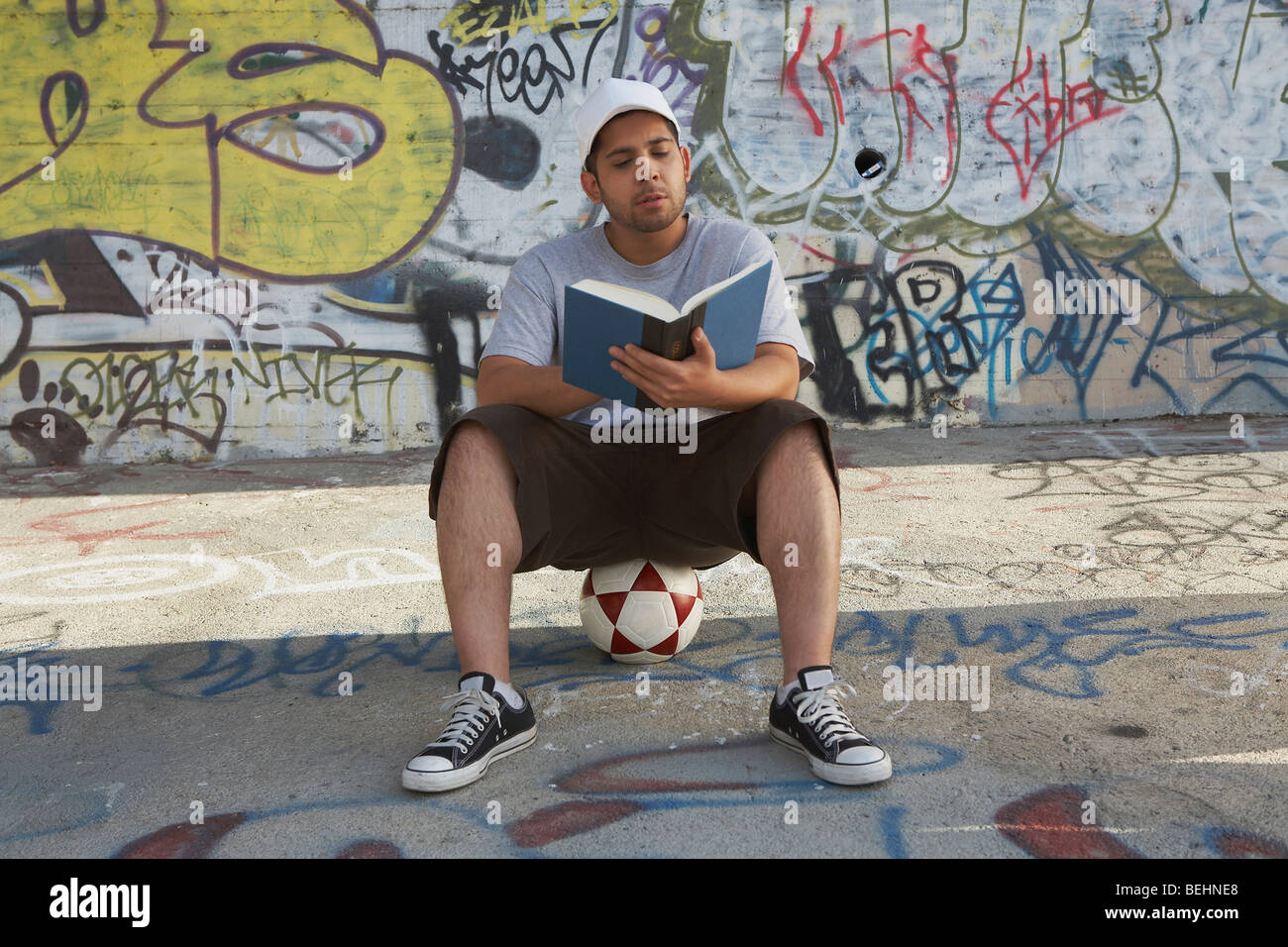 Young man sitting on a soccer ball and reading a book Stock Photo - Alamy
