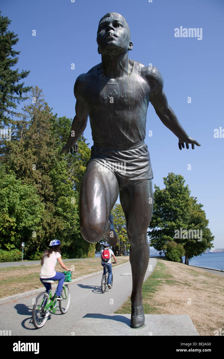 Two people riding past a statue of a running man in Stanley park ...