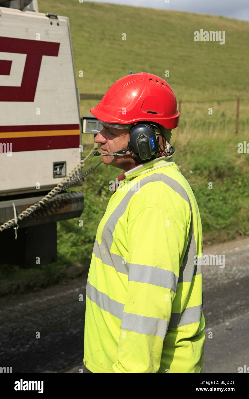 Workman wearing a yellow hi-vis jacket, red safety helmet and a radio ...
