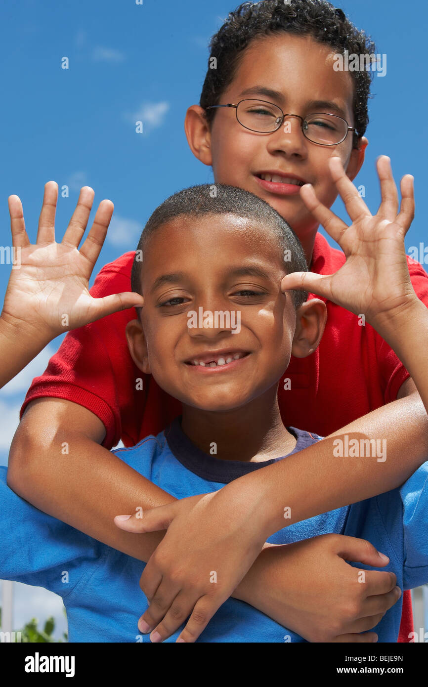 Close-up of a boy making a face with his friend hugging him from behind ...