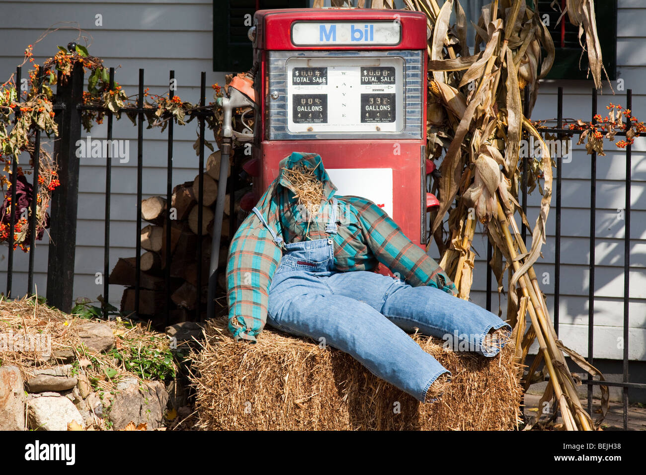 A headless scarecrow sitting on a bale of hay in front of a vintage ...