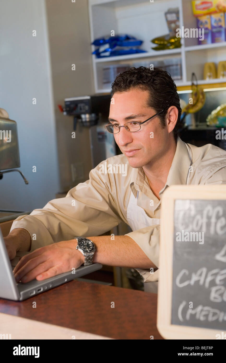 Male store clerk using a laptop in a coffee shop Stock Photo - Alamy
