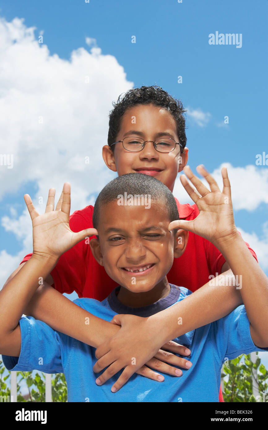 Close-up of a boy making a face with his friend hugging him from behind ...