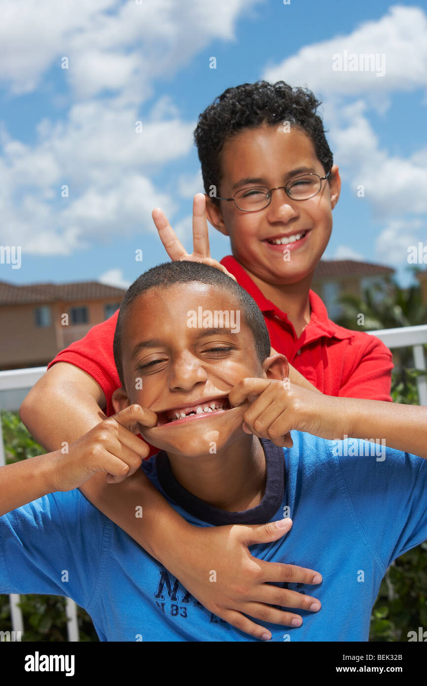 Close-up of a boy making a face with his friend making a gesture of ...