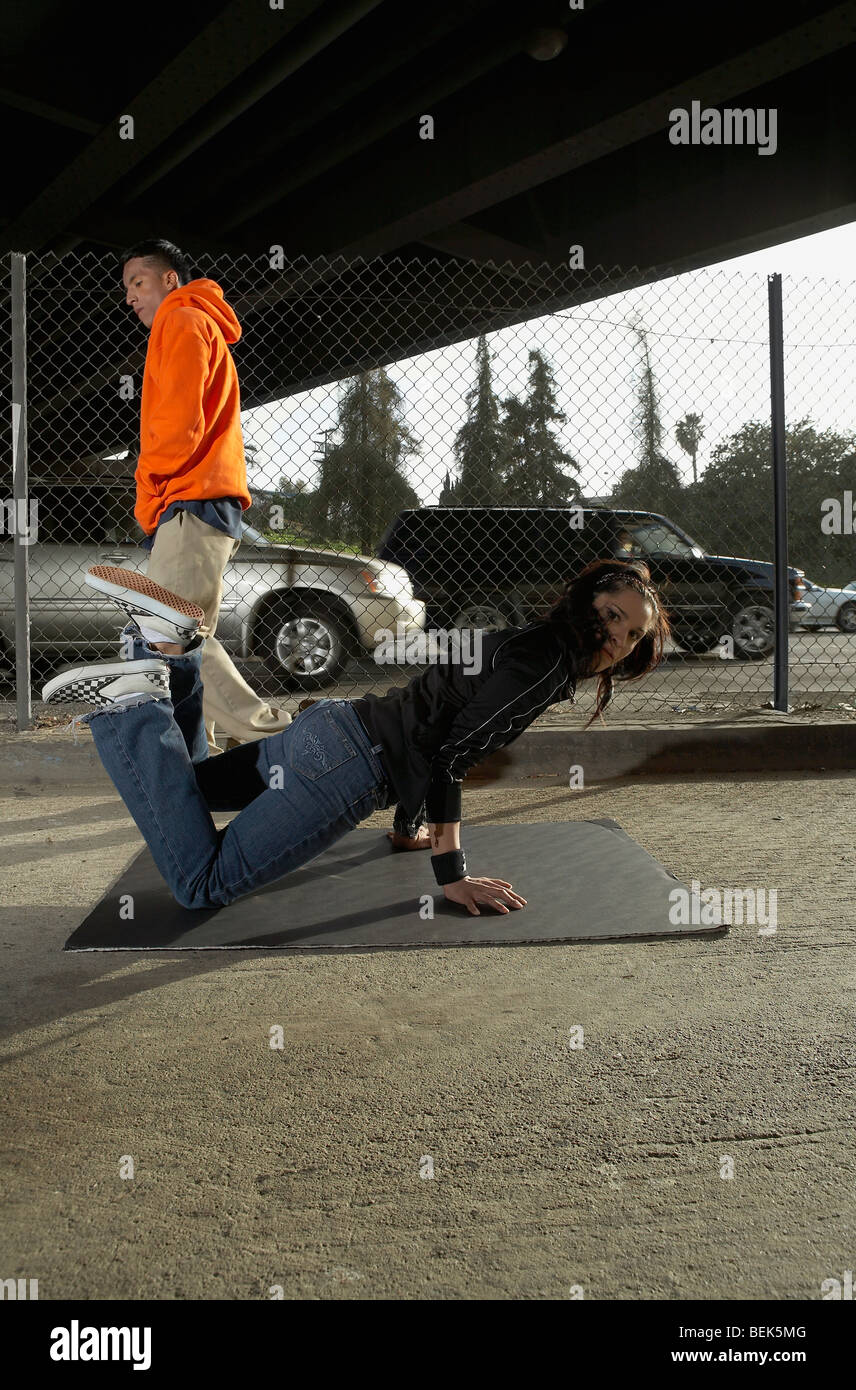 Side profile of a young woman break dancing with a young man standing ...