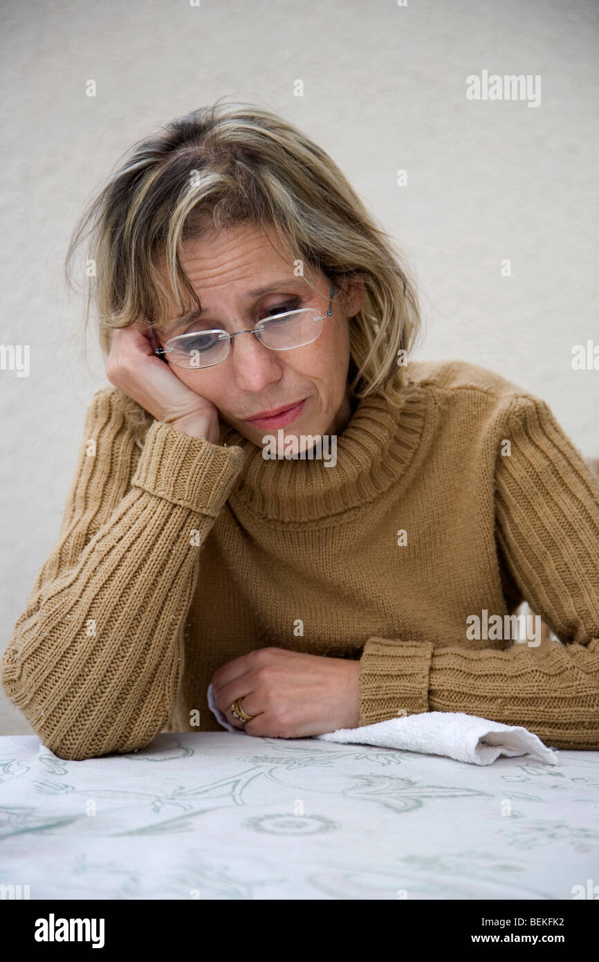 Sad woman in her fifties, sitting at table Stock Photo - Alamy