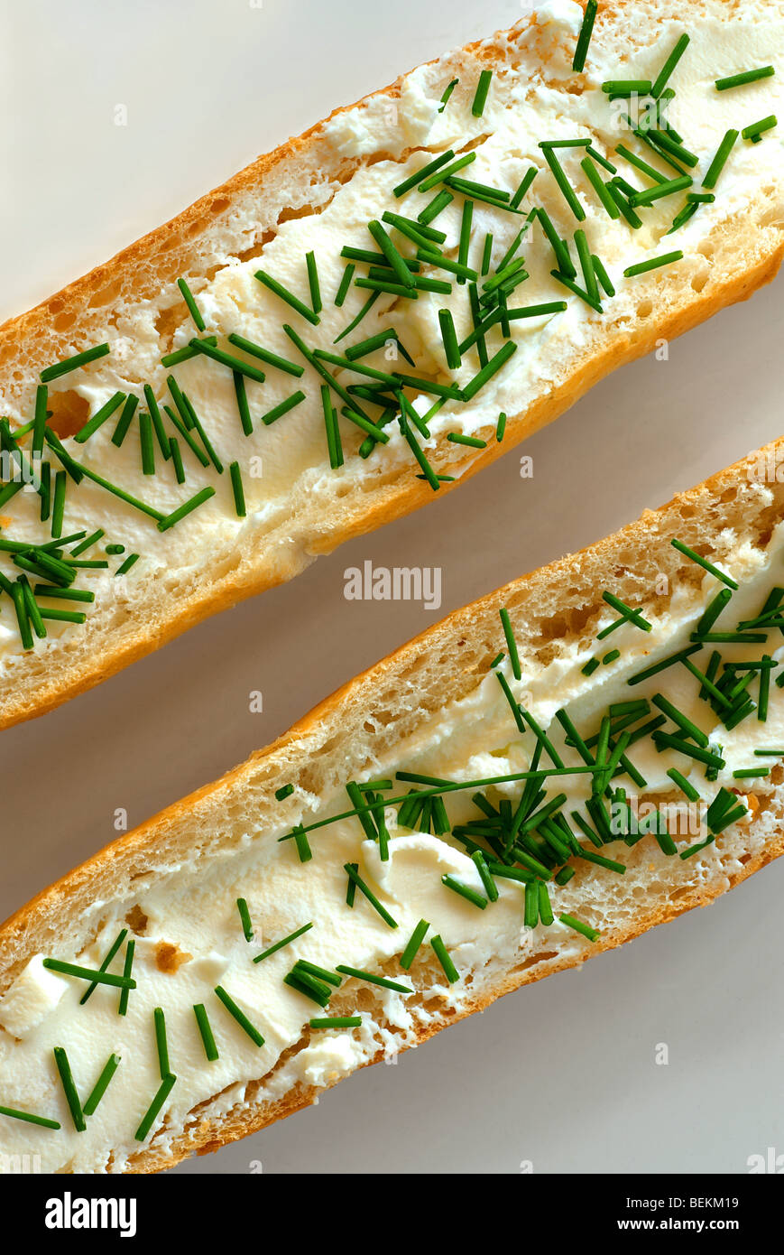 Diagonal composition of two bread rolls with cheese and chives on white ...