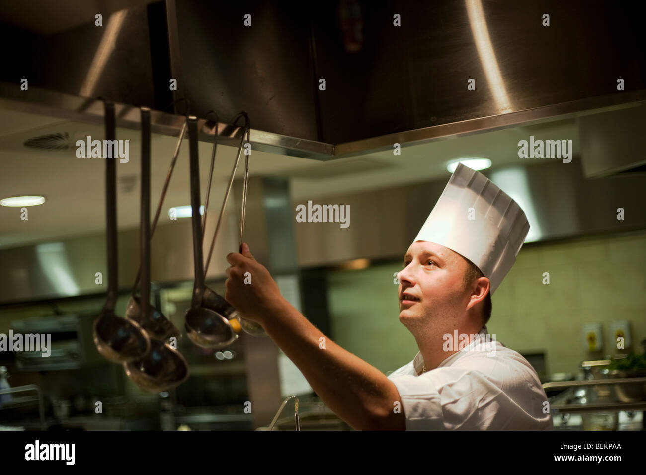 A chef wearing a traditional toque hat reaches for a ladle in hotel ...