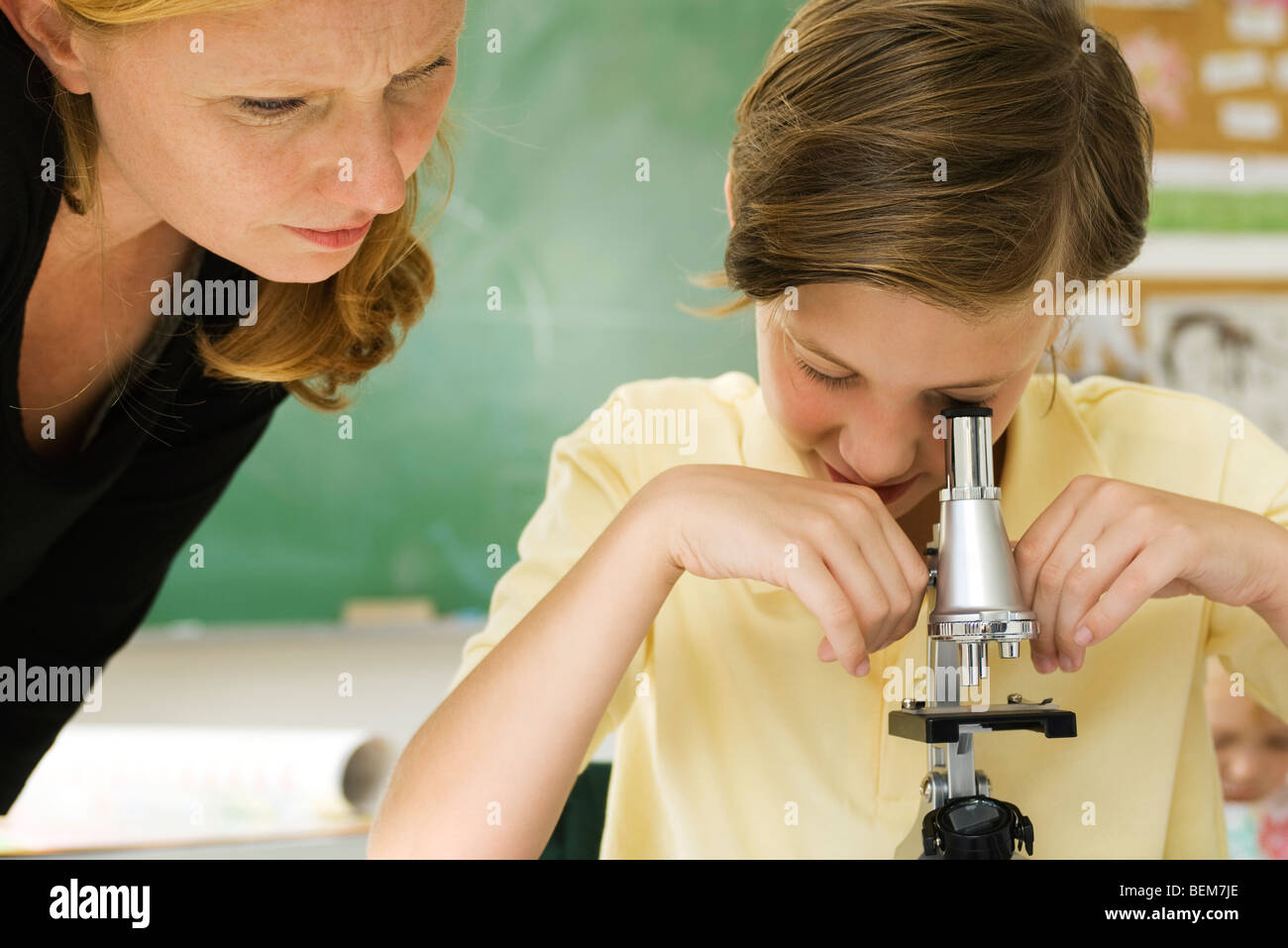 Elementary teacher watching student using microscope Stock Photo - Alamy
