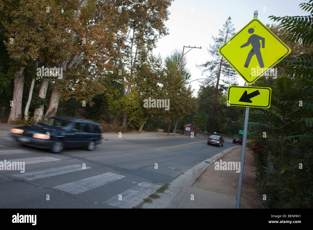 A tilted view of a pedestrian road sign and a crosswalk with cars ...