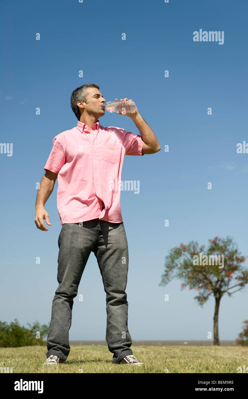Man standing outdoors drinking from bottle of water, low angle view ...