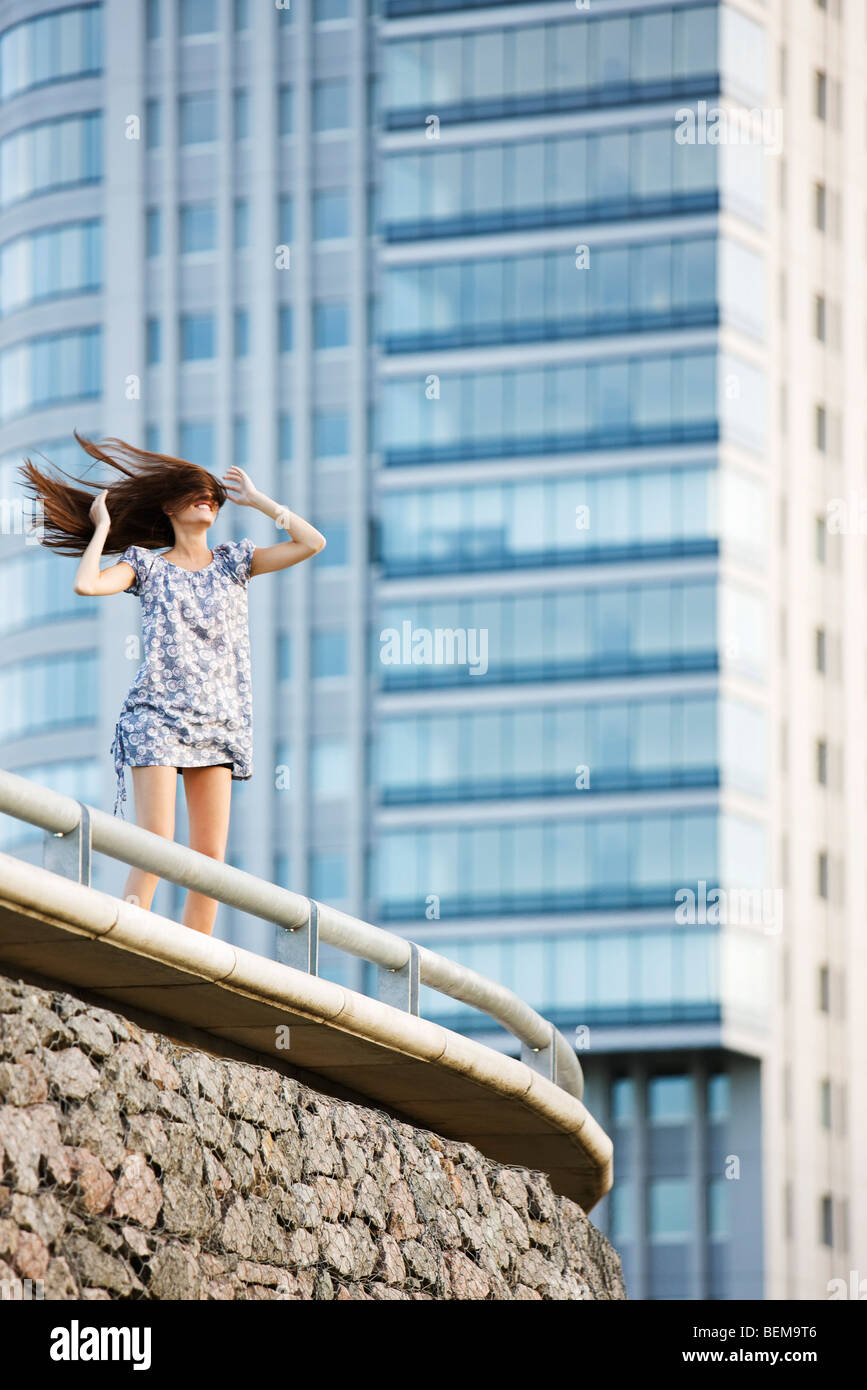 Young woman standing on balcony, wind blowing long hair across face ...