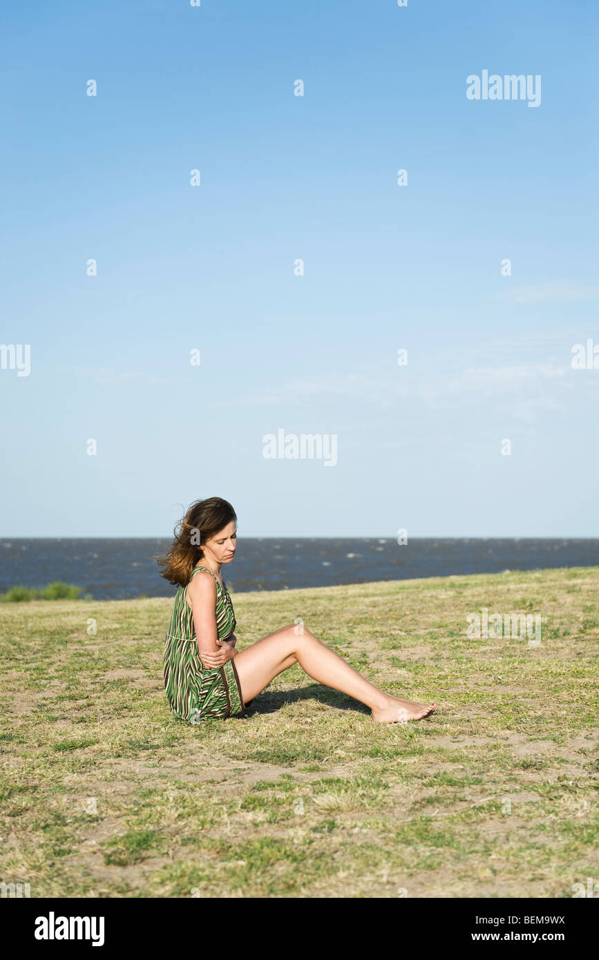 Woman sitting on grass with arms folded over stomach, head down Stock ...