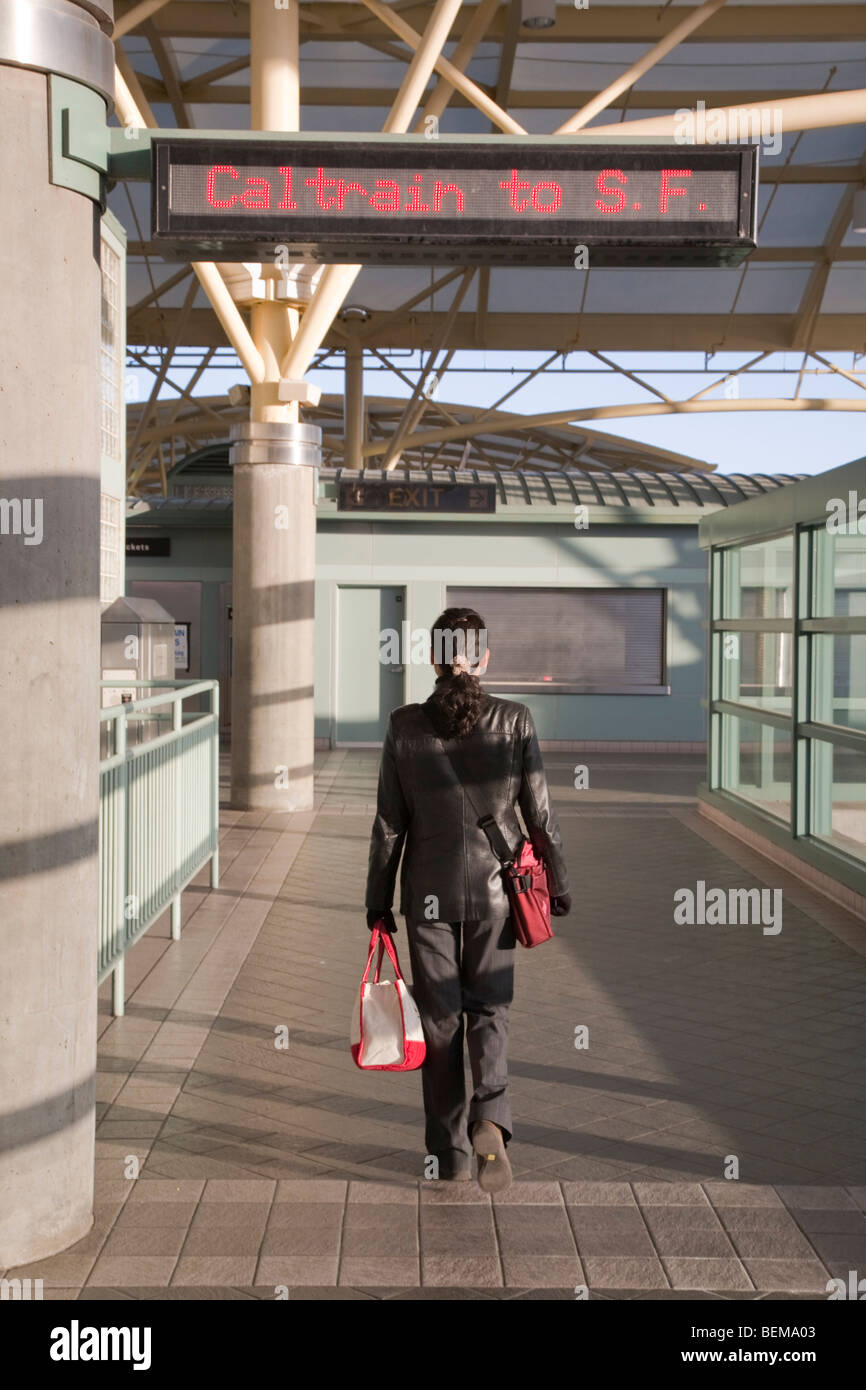 Woman walking below an electronic sign announcing Caltrain service to ...