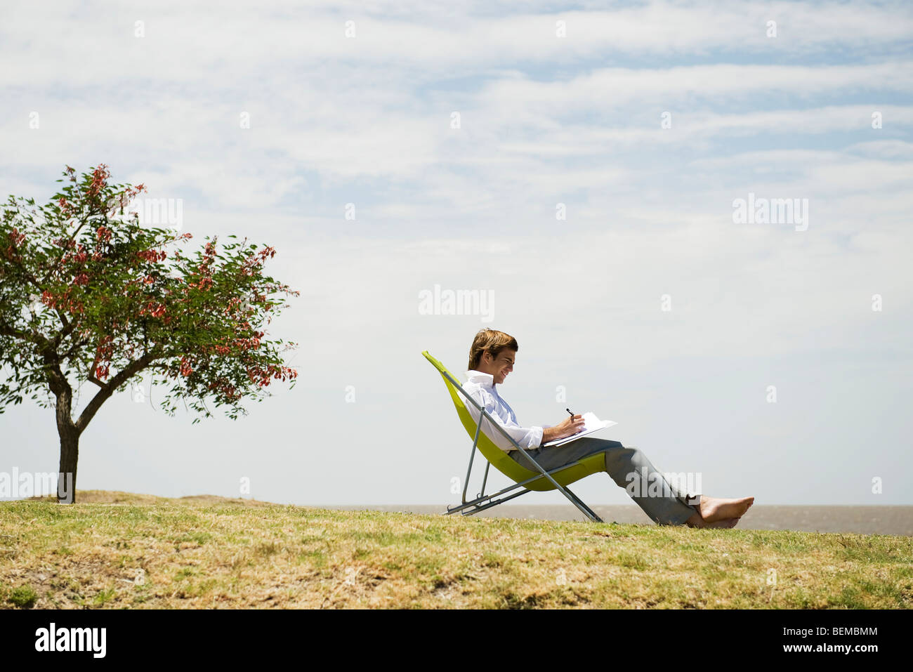 Man relaxing in lounge chair outdoors writing in notebook Stock Photo ...