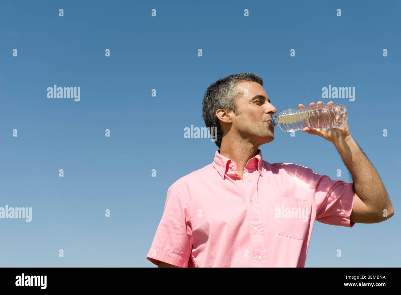 Man standing outdoors drinking from bottle of water, low angle view ...