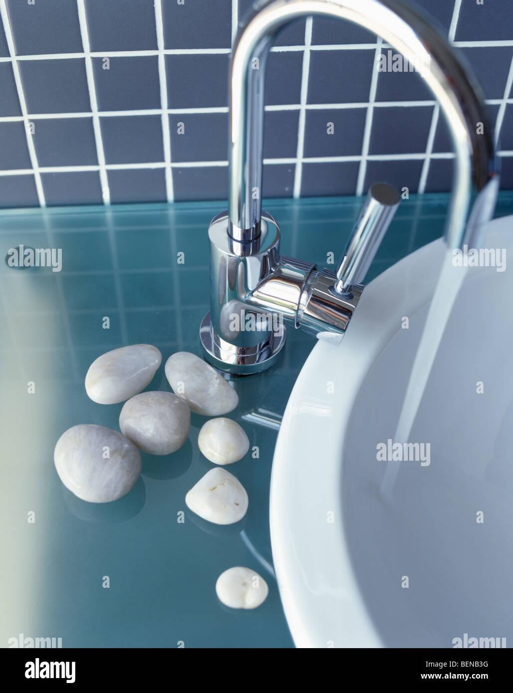 Close-up of pebbles on glass unit with mixer tap pouring water into ...