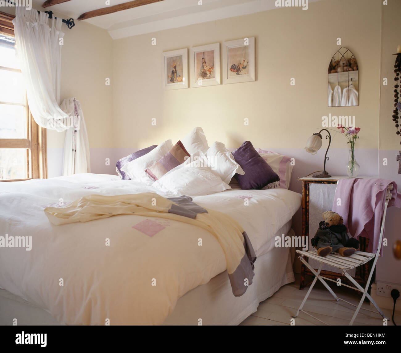 Bed piled with pillows in cream country bedroom with clothes thrown ...