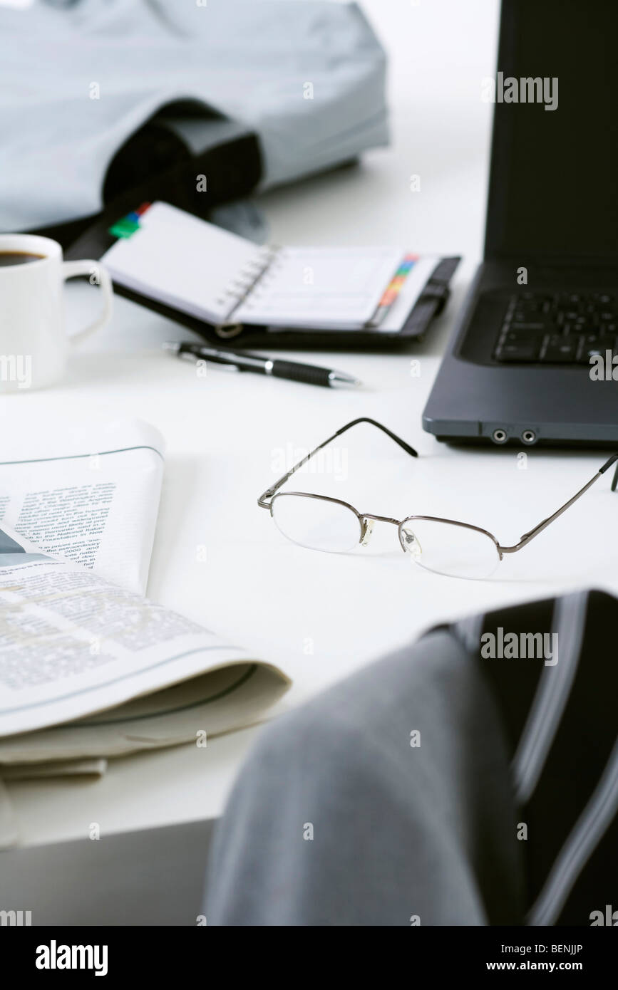Glasses, newspaper and laptop computer on cluttered desk Stock Photo ...