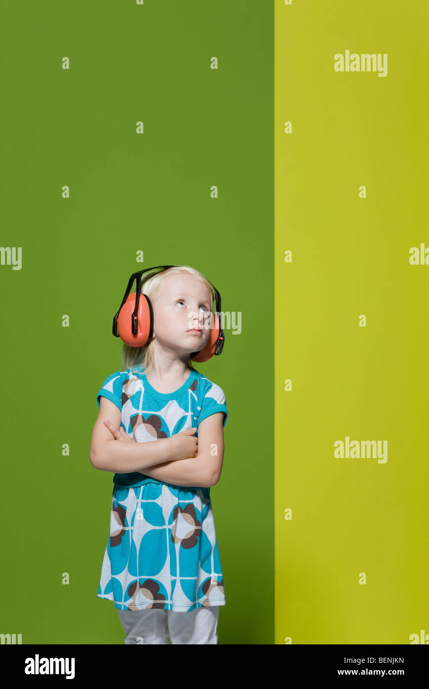 Little girl with arms folded, wearing protective headphones, defiantly ...