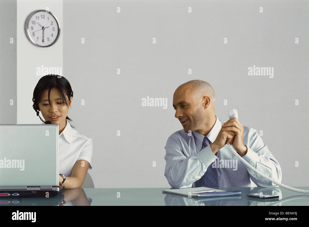 Office worker sitting at desk holding phone, covering receiver and ...