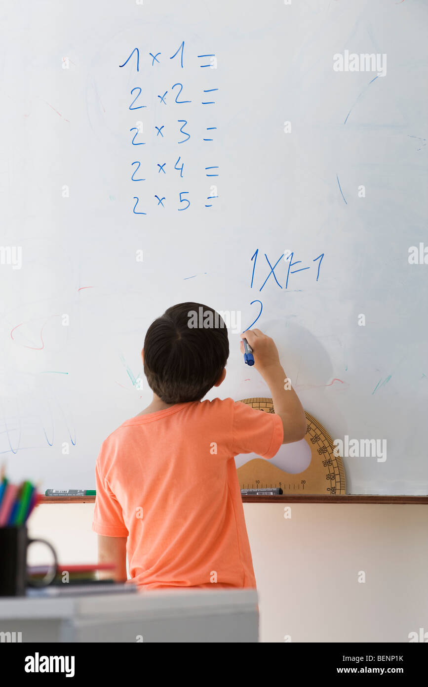 Elementary school student doing math equation on whiteboard, rear view ...
