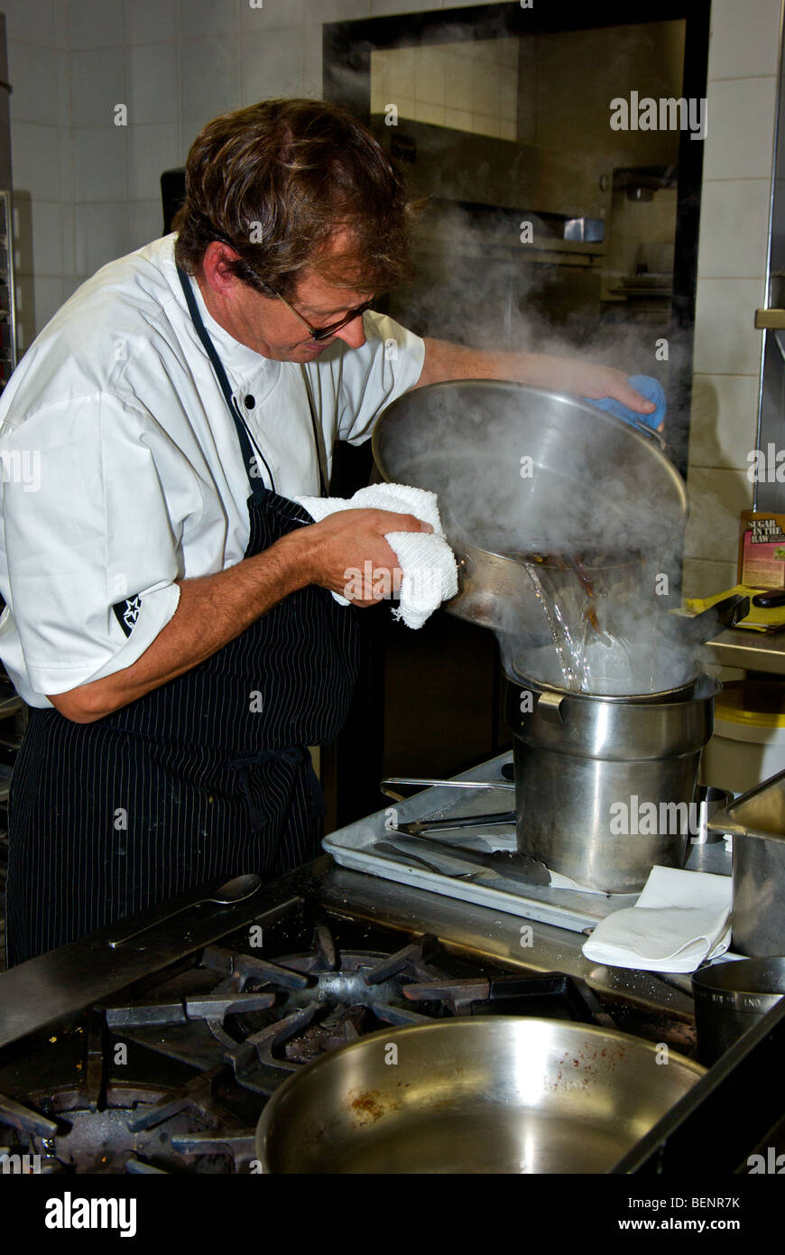 Chef straining steaming hot clear soup through sieve in commercial ...