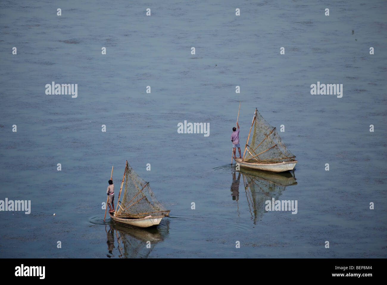Two fishermen in boats with traditional cone fishing nets use poles to ...