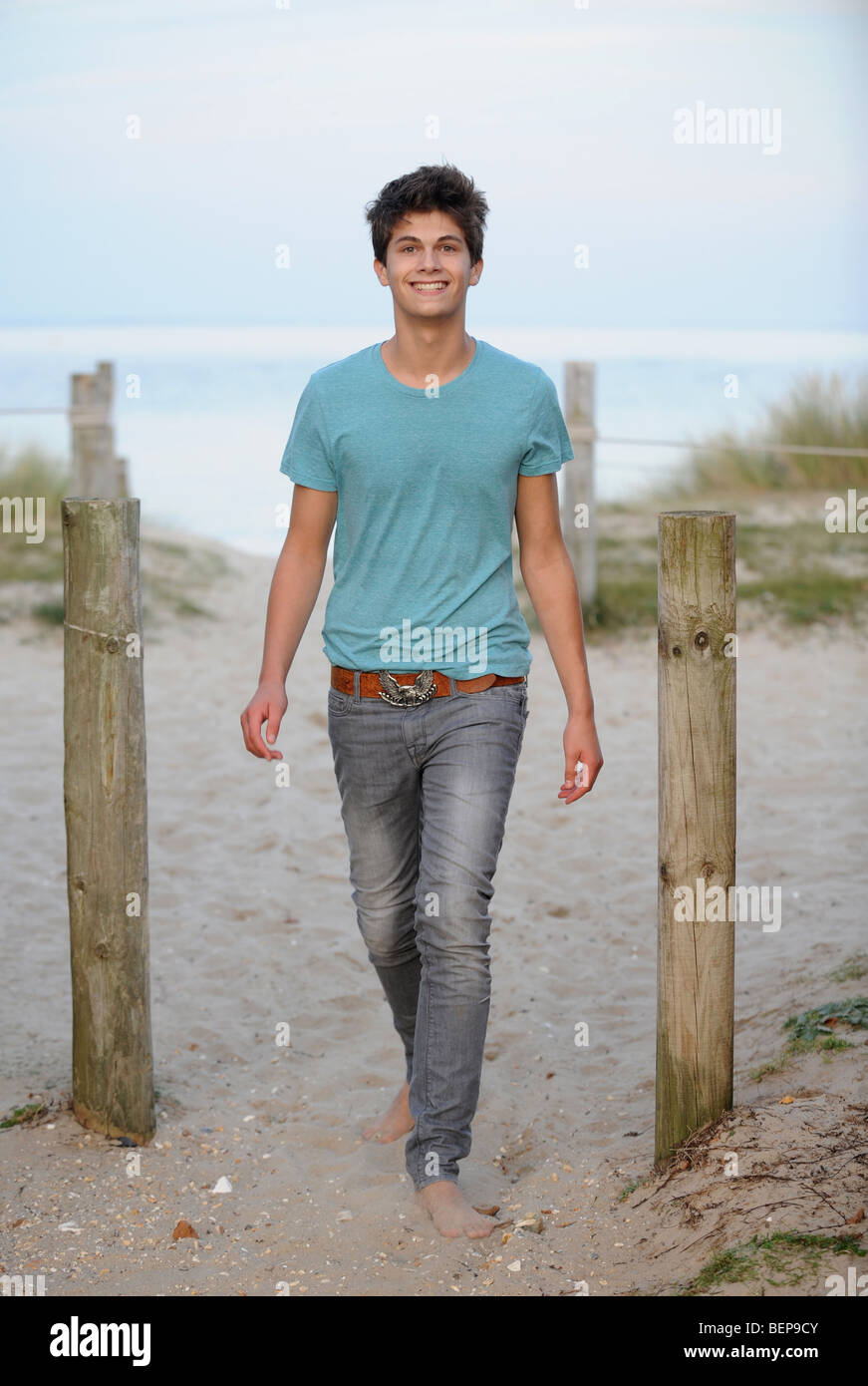 Good looking, handsome Teenage boy standing by wooden post on sandy ...
