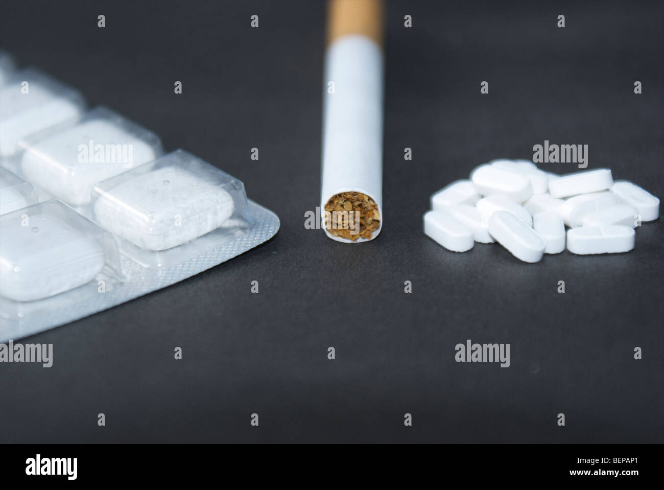 A cigarette, nicotine gum and anti-smoking pills on a black background ...