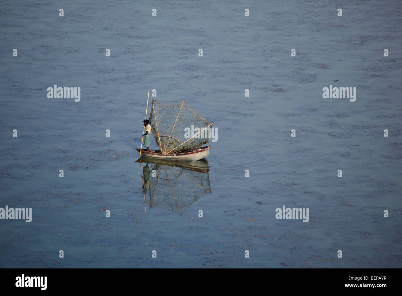 A fisherman in with a traditional cone fishing net use a pole to ...